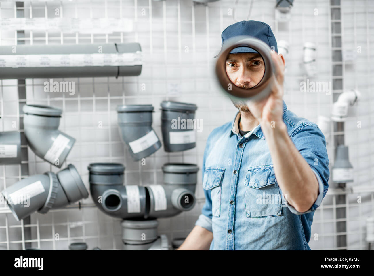 Funny portrait of a handsome workman choosing sewer pipes standing near ...