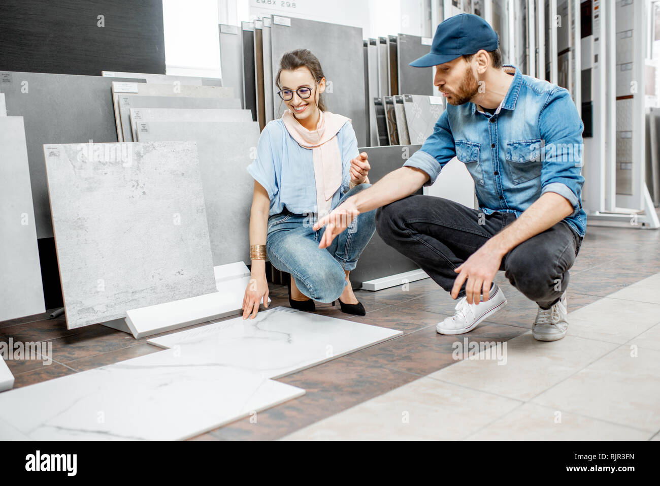 Young woman customer choosing tiles standing with seller or repairman ...