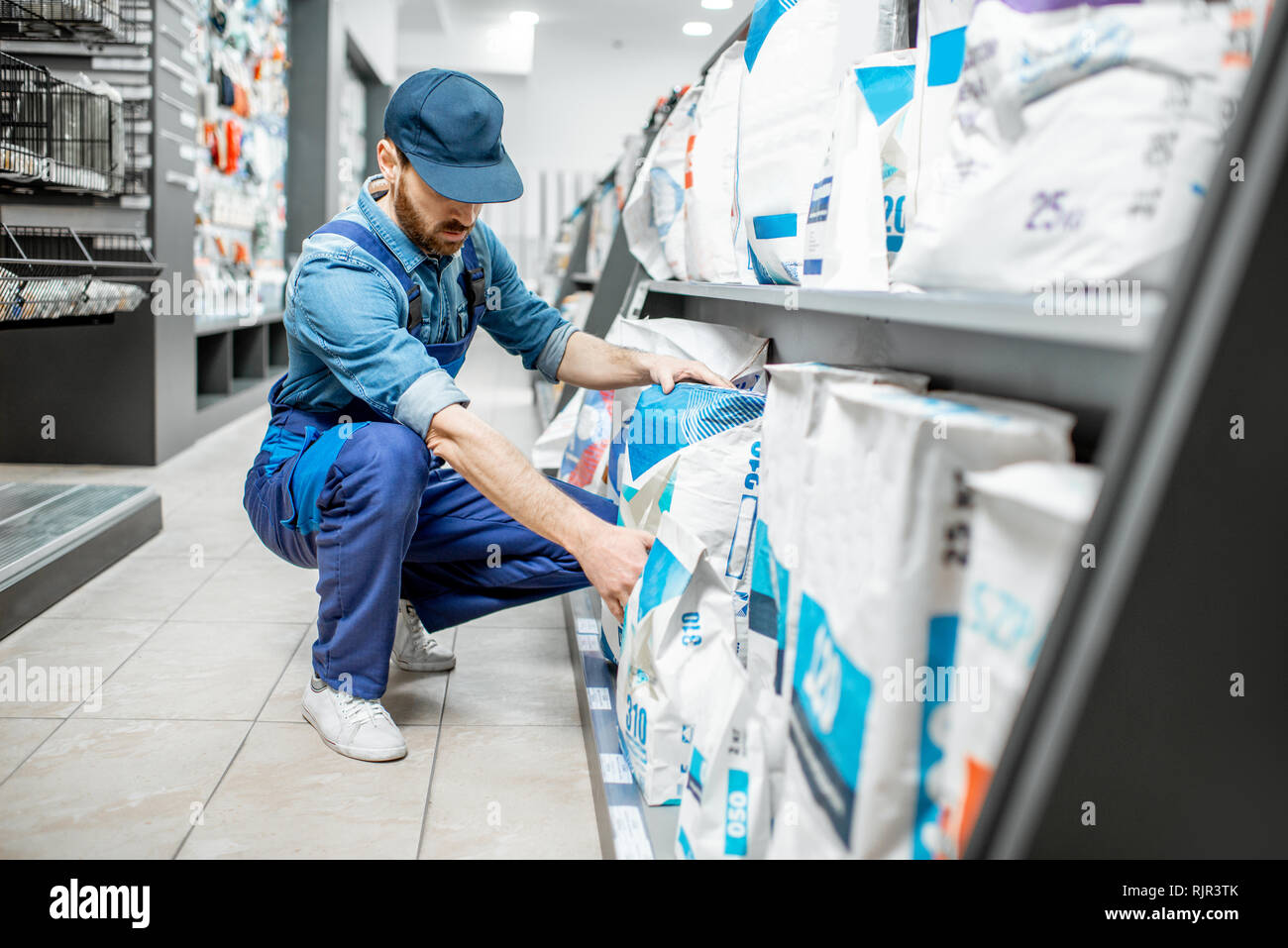 Workman in blue overalls taking a bag with construction mixture, buying ...