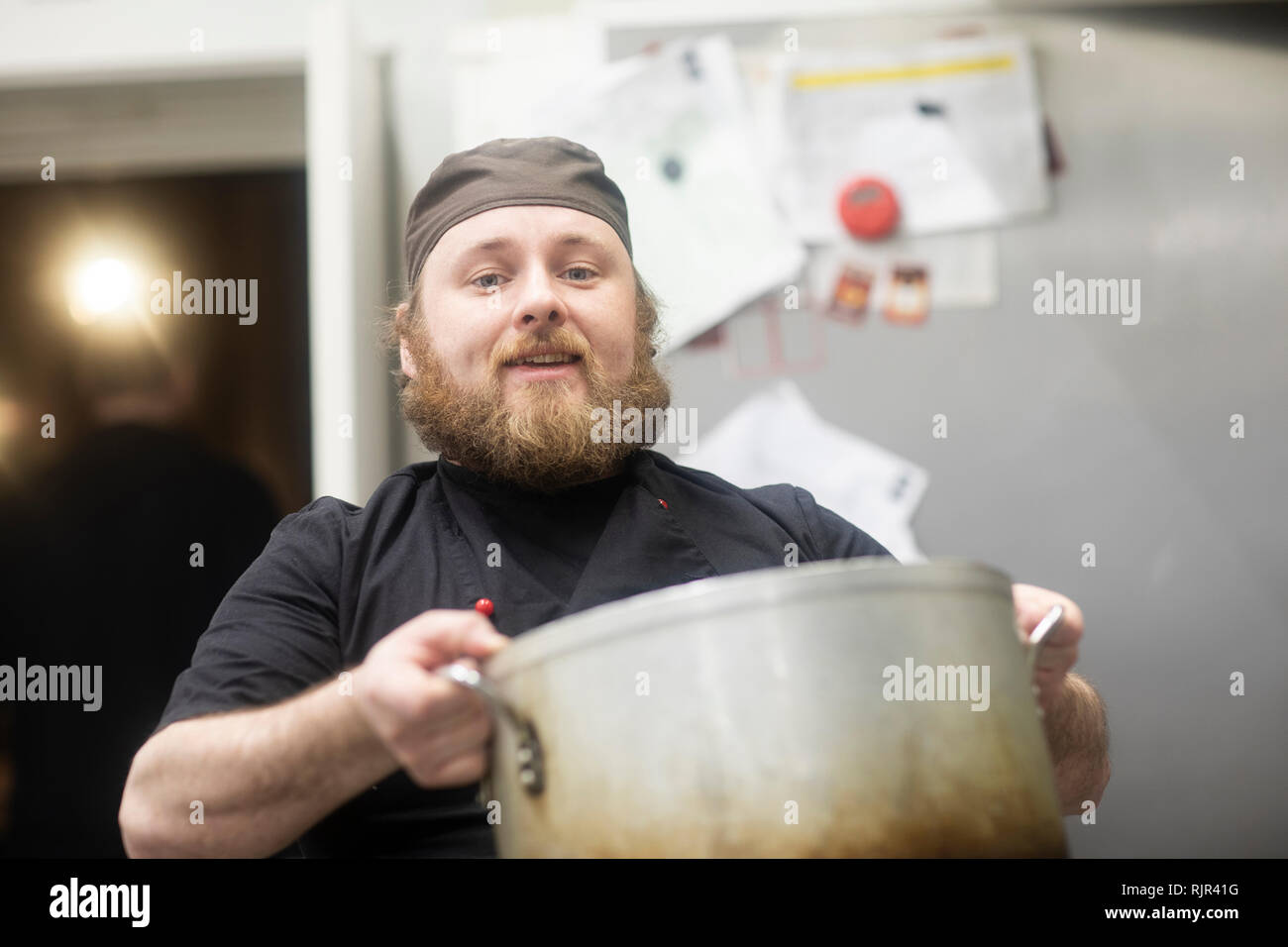 Fast food worker carrying large pan in commercial kitchen, portrait ...