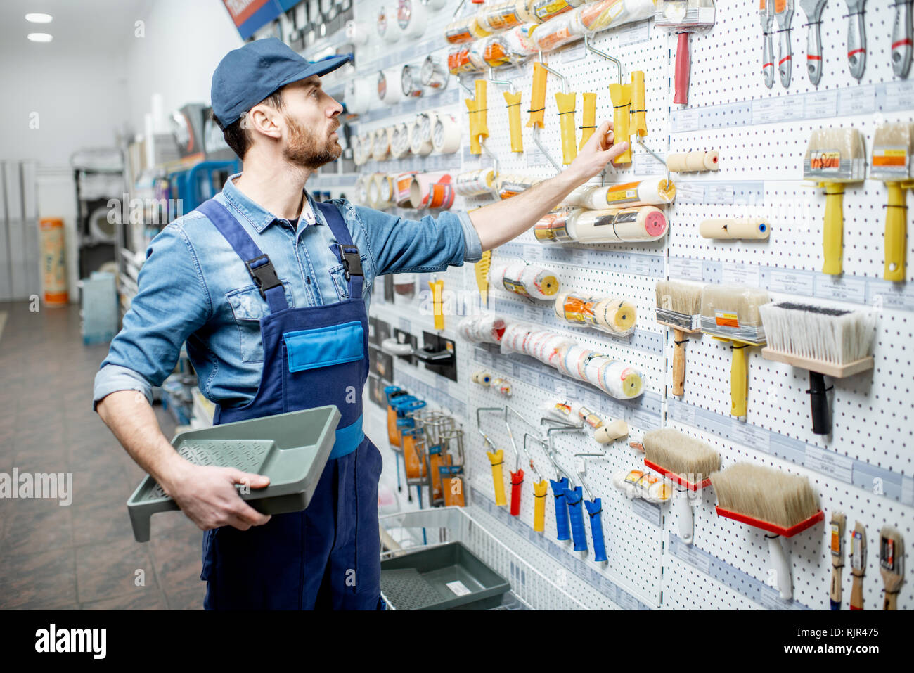 Handsome workman in uniform choosing tools for painting in the building ...