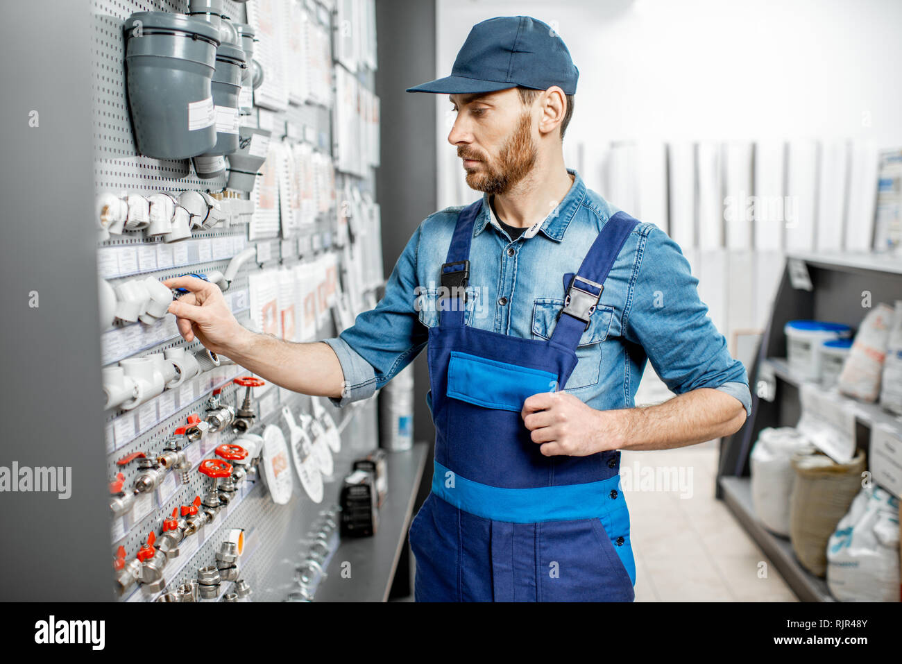 Handsome workman choosing water pipes and pipe joints standing near the ...