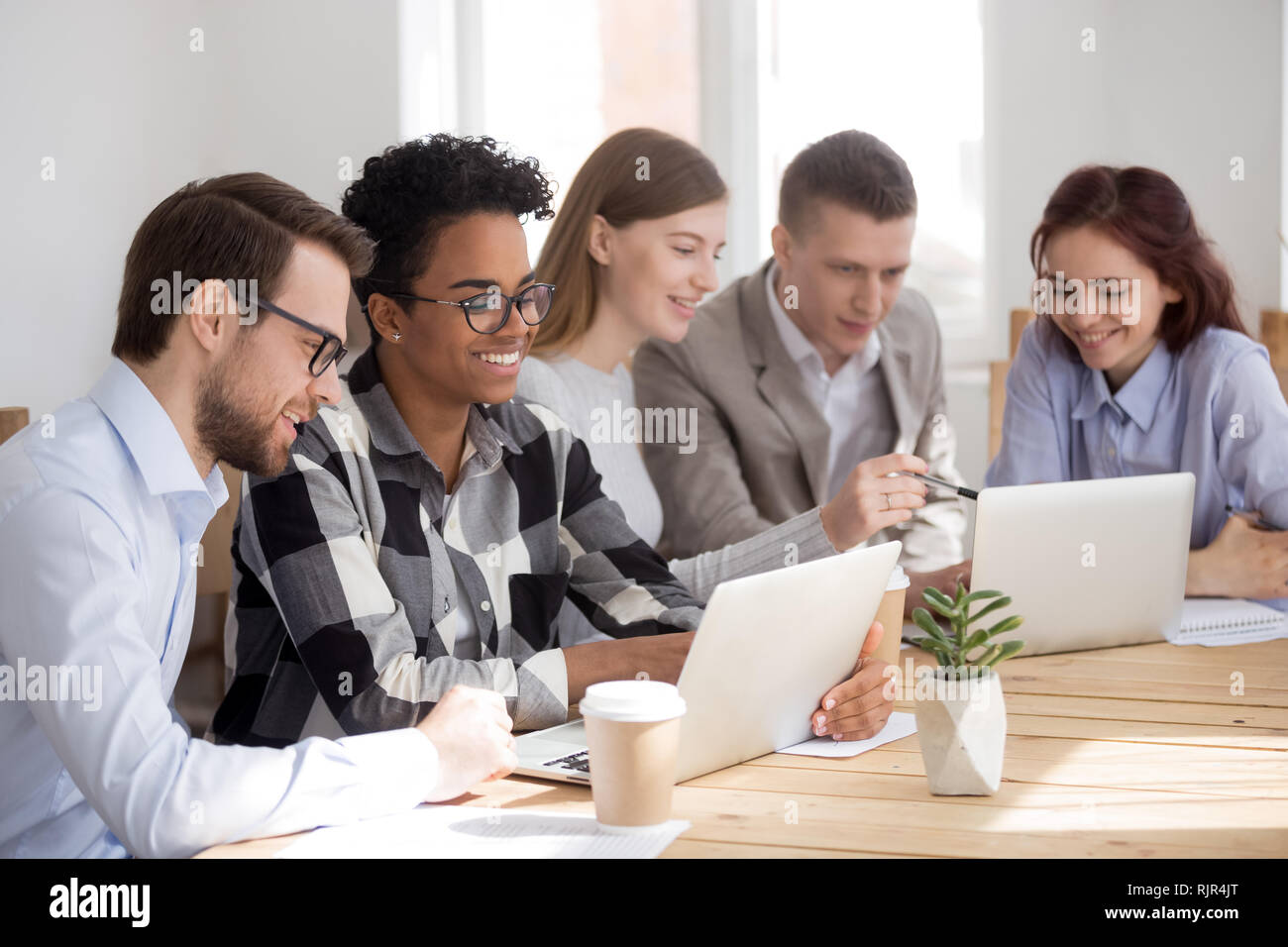 Happy diverse research team working on laptops cooperating ...