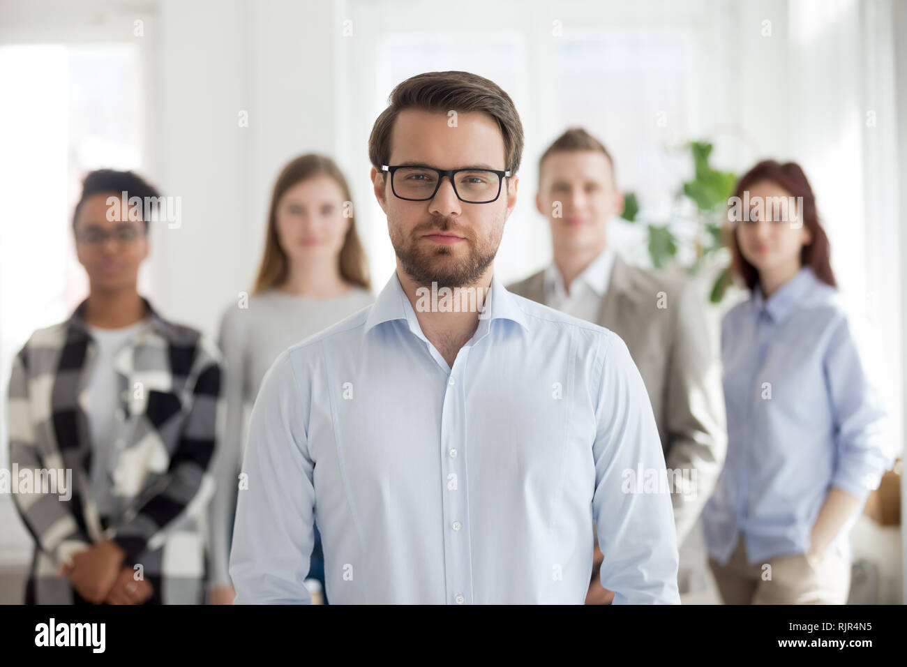 Serious confident businessman looking at camera with team at background ...