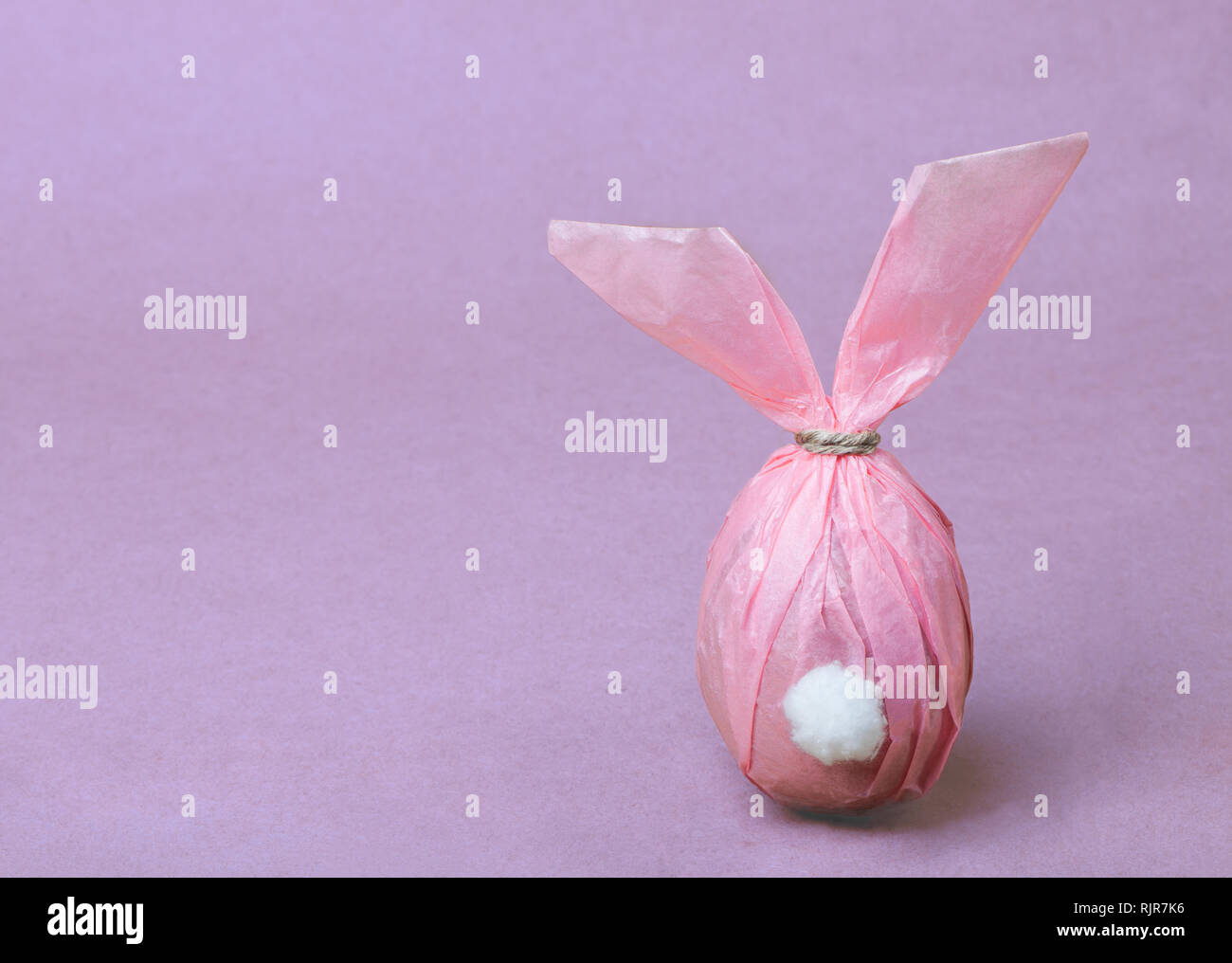 Easter egg in the form of a cute pink Easter bunny on a gentle purple ...
