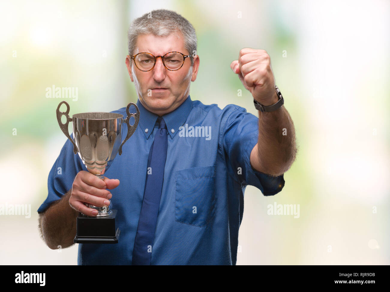 Handsome senior successful man holding trophy over isolated background ...