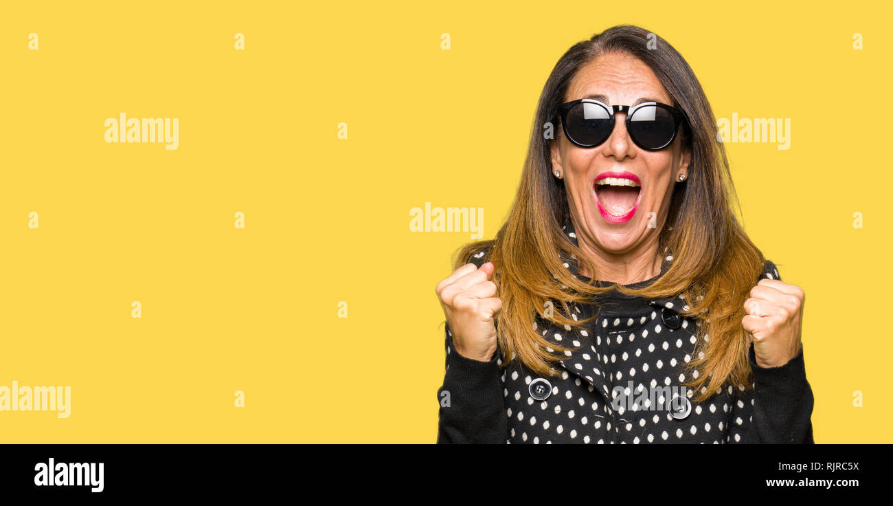 Beautiful middle age woman wearing sunglasses celebrating surprised and ...
