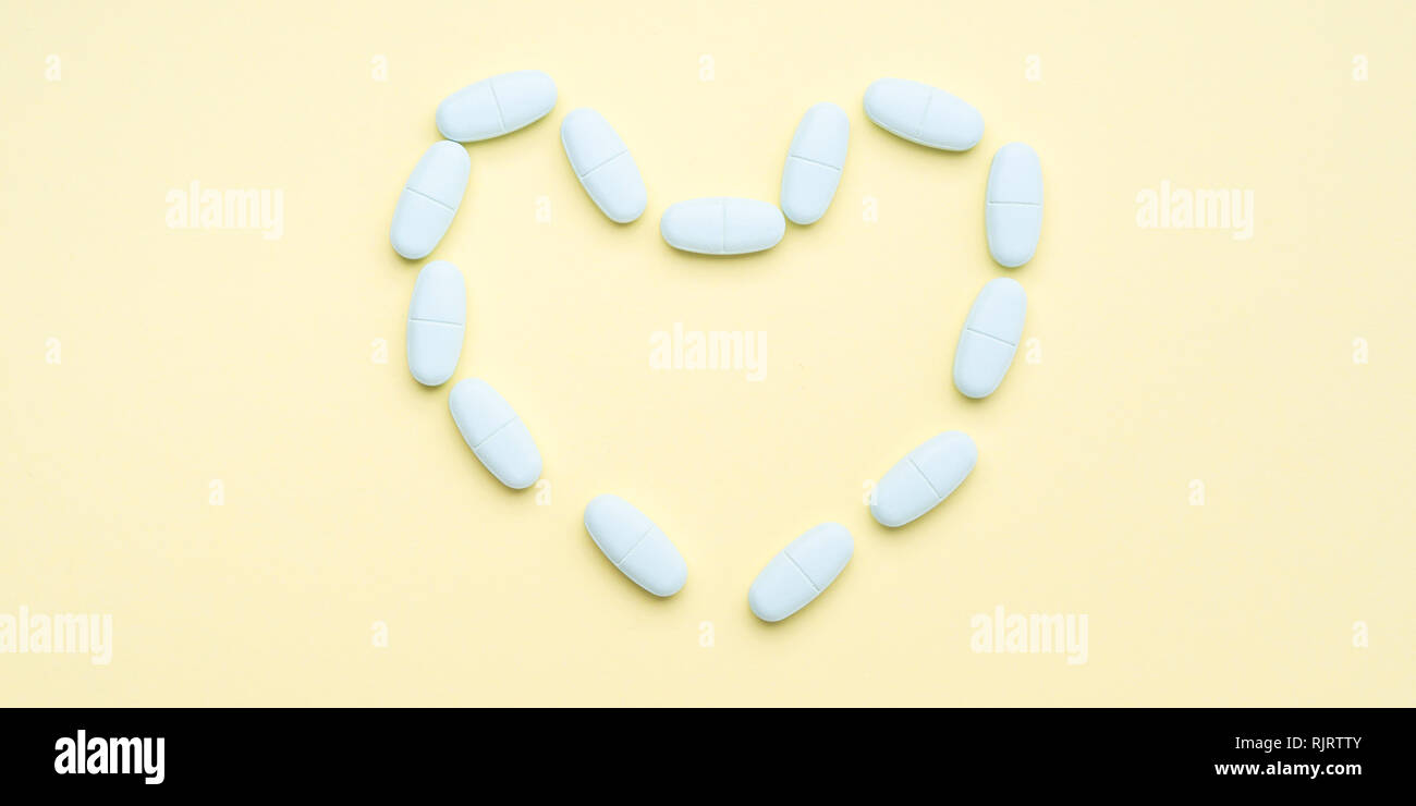 Blue pills forming heart shape on pastel yellow background. Health ...