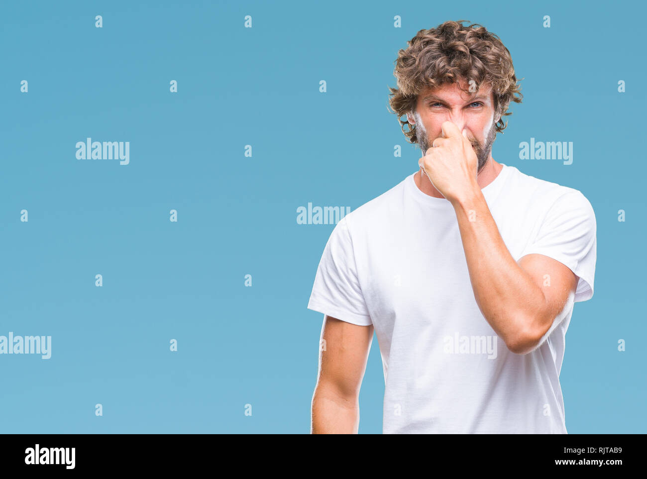 Handsome hispanic model man over isolated background smelling something ...
