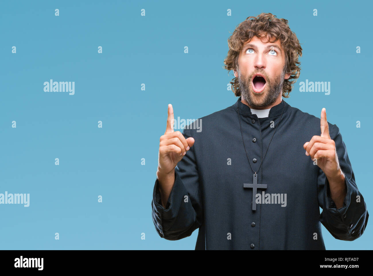 Handsome hispanic catholic priest man over isolated background amazed ...