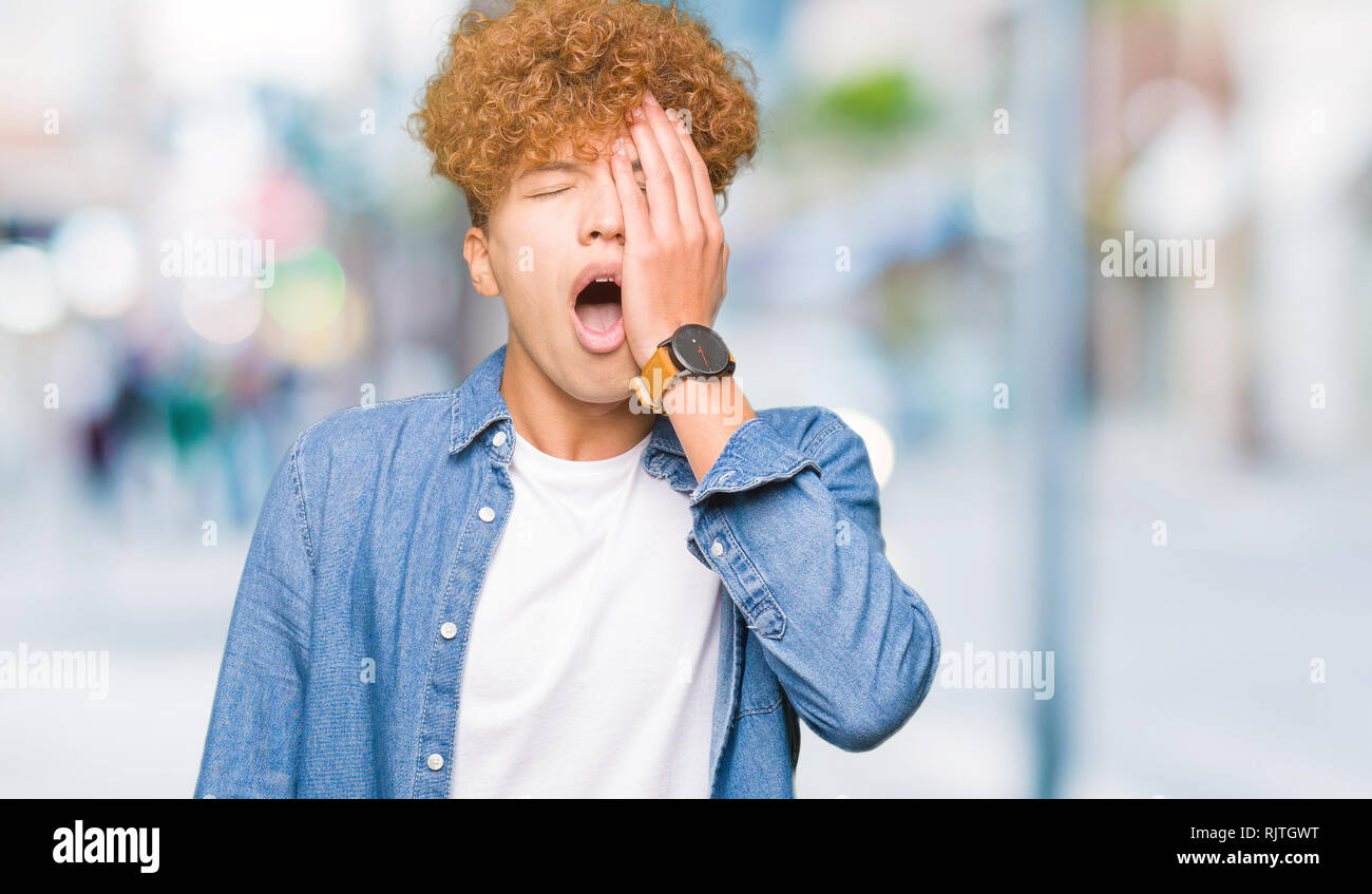 Young handsome man with afro hair wearing denim jacket Yawning tired ...