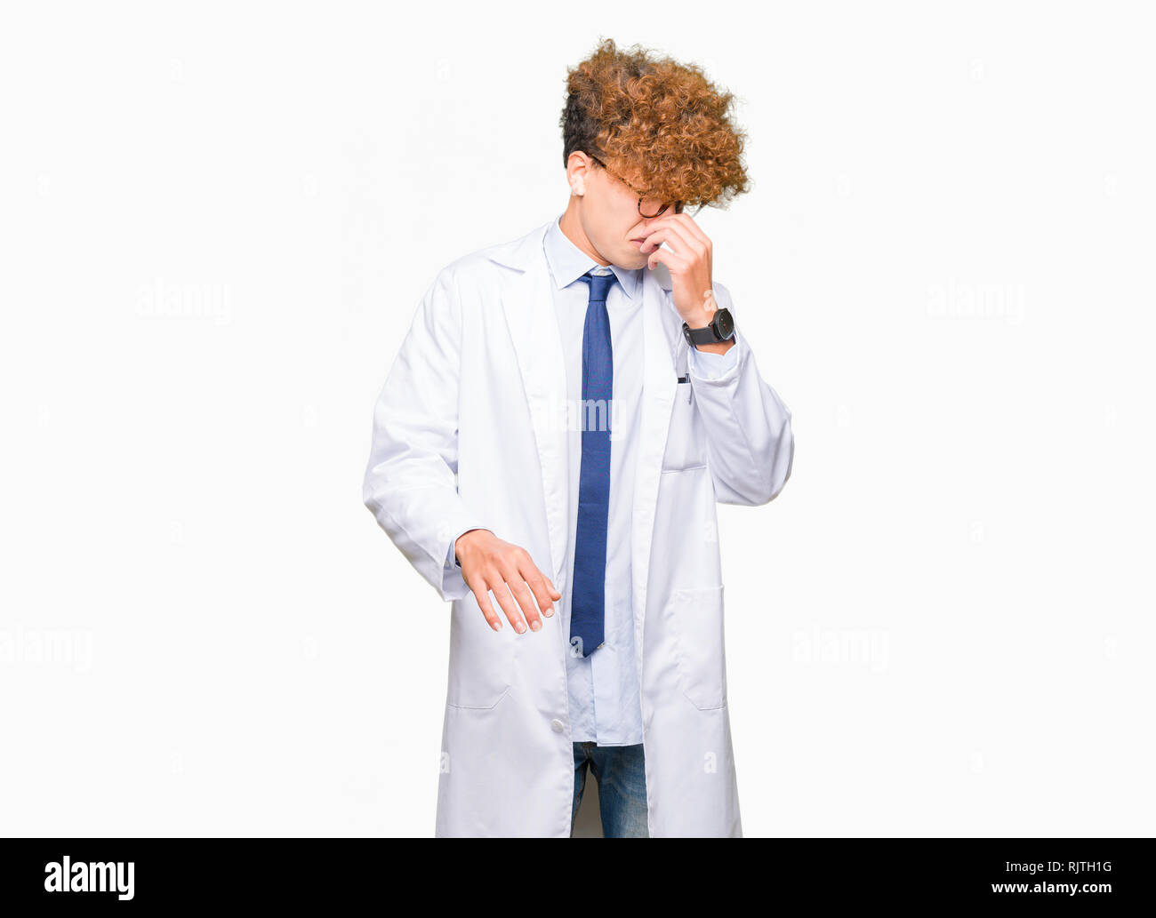 Young handsome scientist man wearing glasses smelling something stinky ...