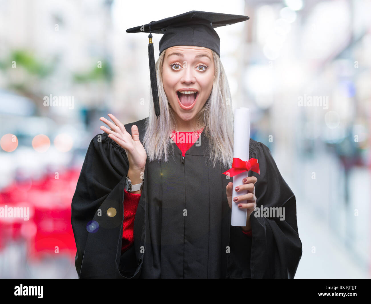 Young blonde woman wearing graduate uniform holding degree over ...