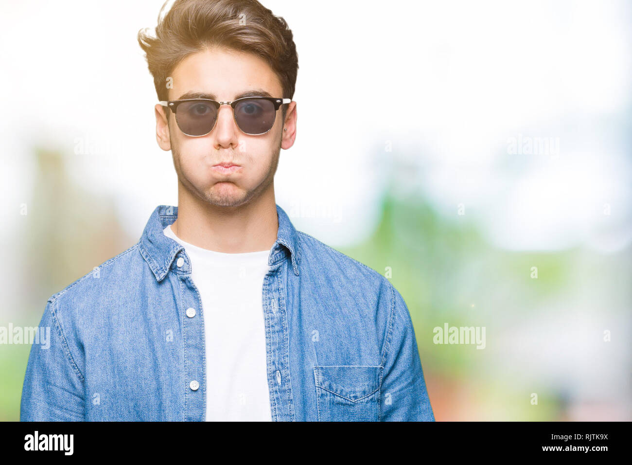 Young handsome man wearing sunglasses over isolated background puffing ...