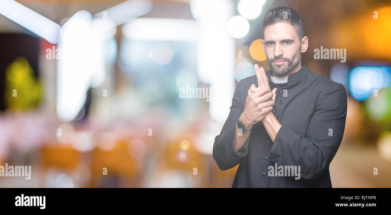Young Christian priest over isolated background Holding symbolic gun ...