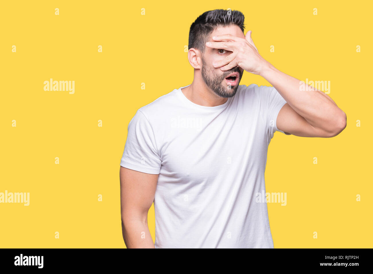 Young man wearing casual white t-shirt over isolated background peeking ...