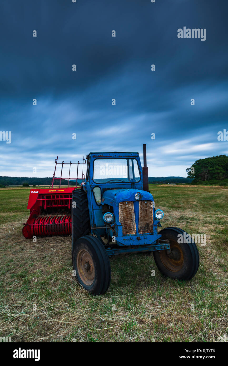Red and blue tractor in field with stormy sky, Halland, Sweden, Europe ...