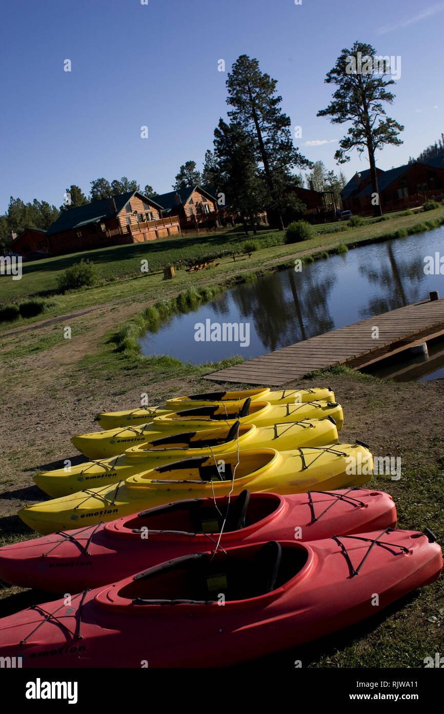 A collection of colorful kayaks sit next to a lake with cabins in the ...