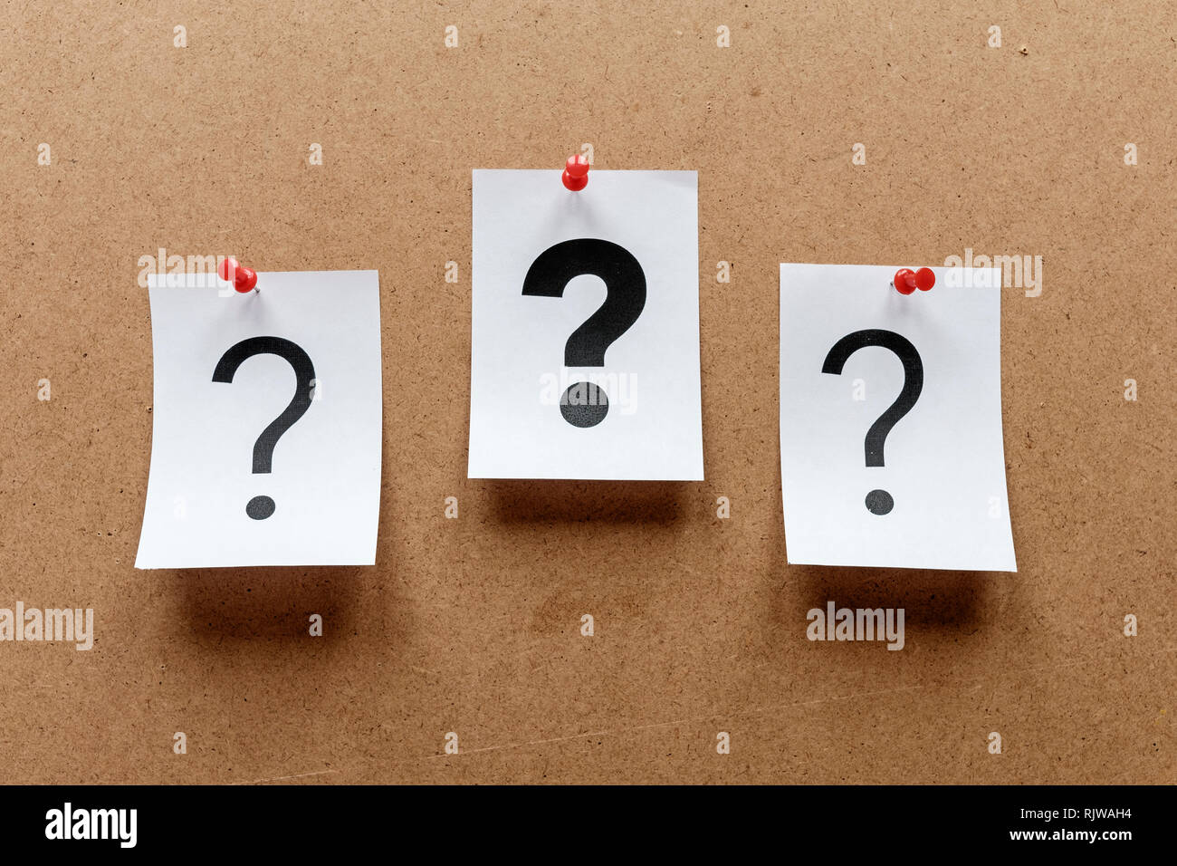 Three question marks pinned to a wooden notice board with a bold one in ...