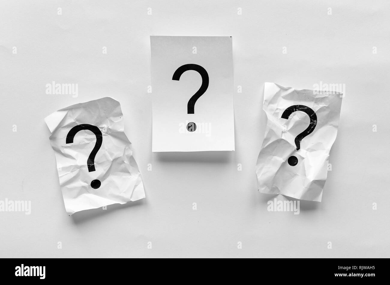 Three question marks on white paper with two crumpled up flanking one ...