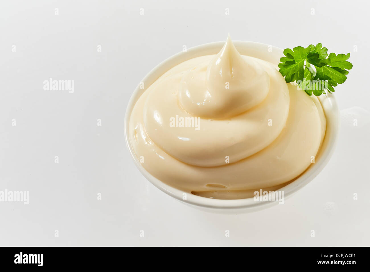 Small bowl of twirled spicy mayonnaise garnished with a leaf of fresh ...