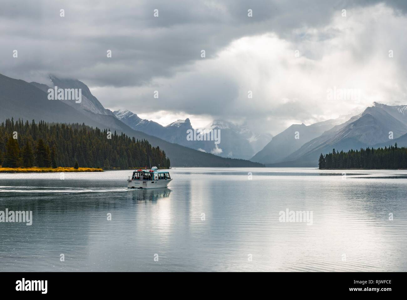 Excursion boat with tourists on Maligne Lake, behind it mountain range ...
