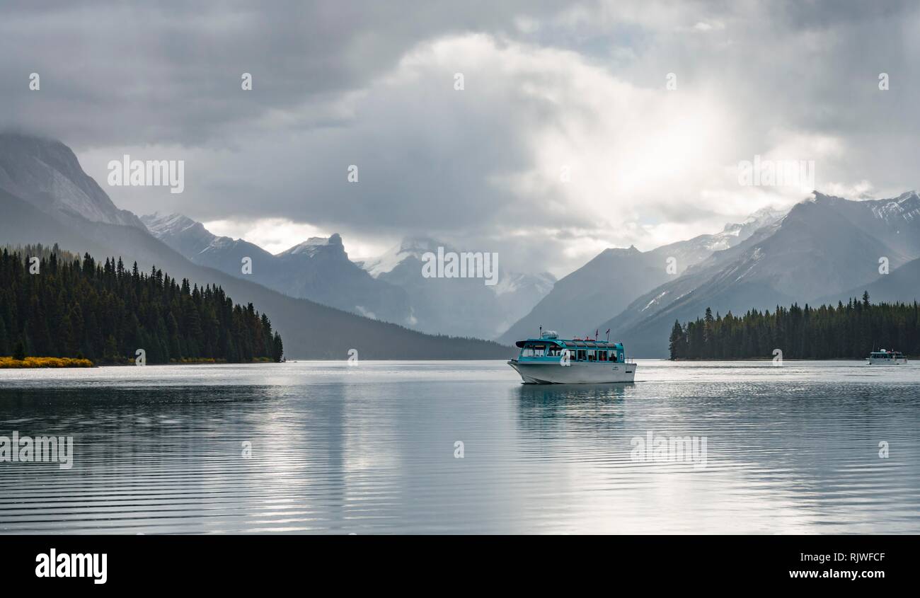 Excursion boat with tourists on Maligne Lake, behind it mountain range ...