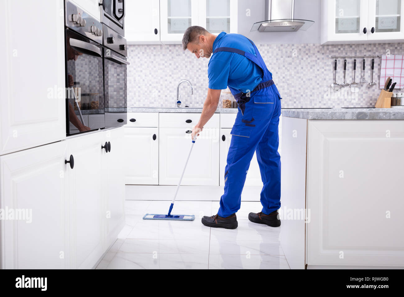 Side View Of A Male Janitor Cleaning White Floor With Mop In The ...