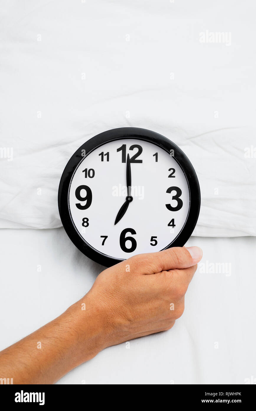 closeup of the hand of a young caucasian man grabbing a clock at seven ...
