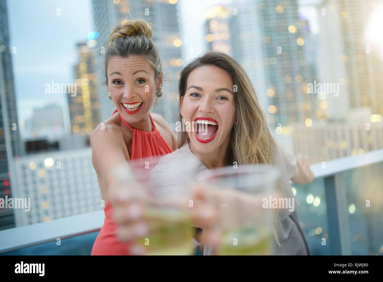 Two gorgeous friends having fun on rooftop bar in city at night fall ...