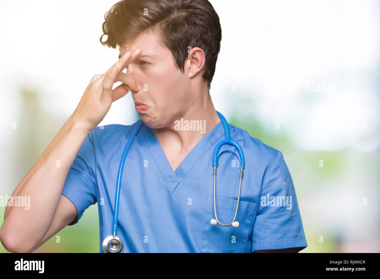 Young doctor wearing medical uniform over isolated background smelling ...