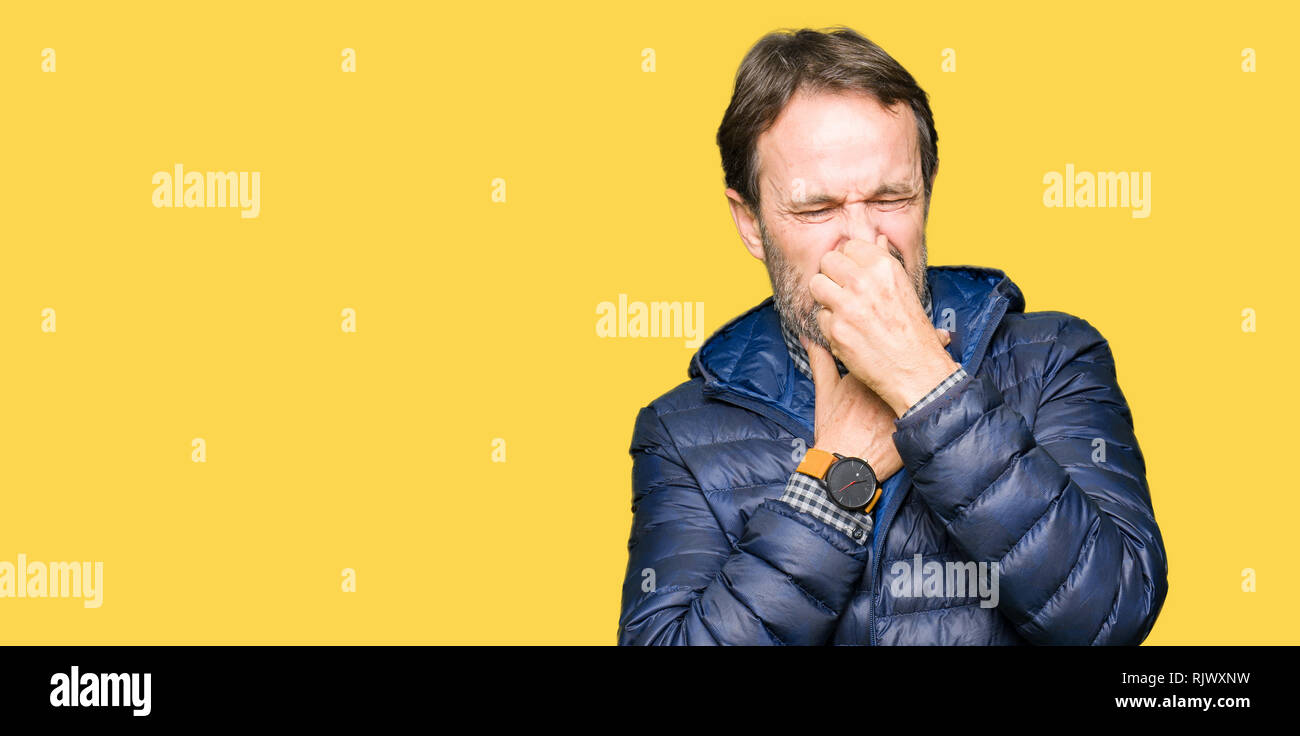 Middle age handsome man wearing winter coat smelling something stinky ...
