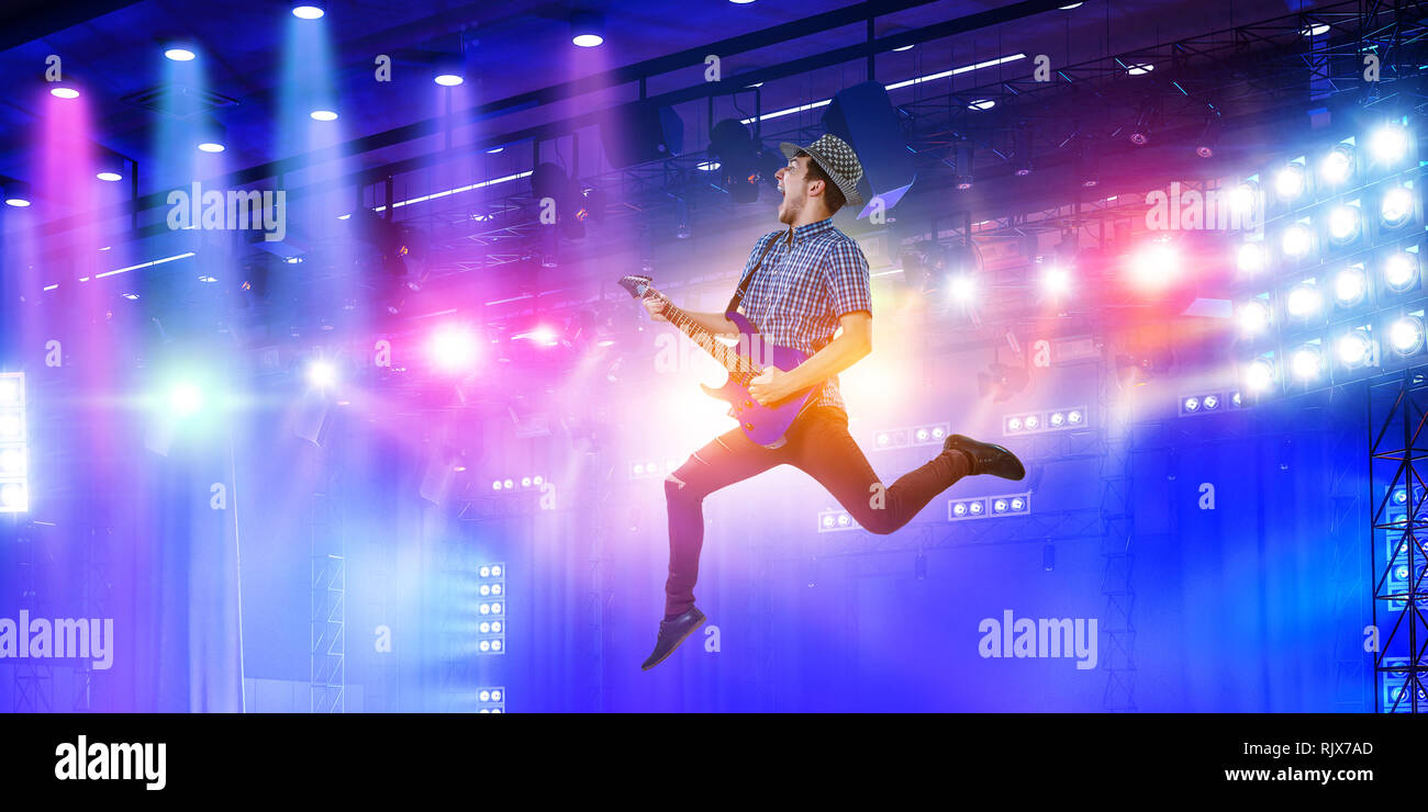 Guitarist jumping high on stage and spotlights at background. Mixed ...