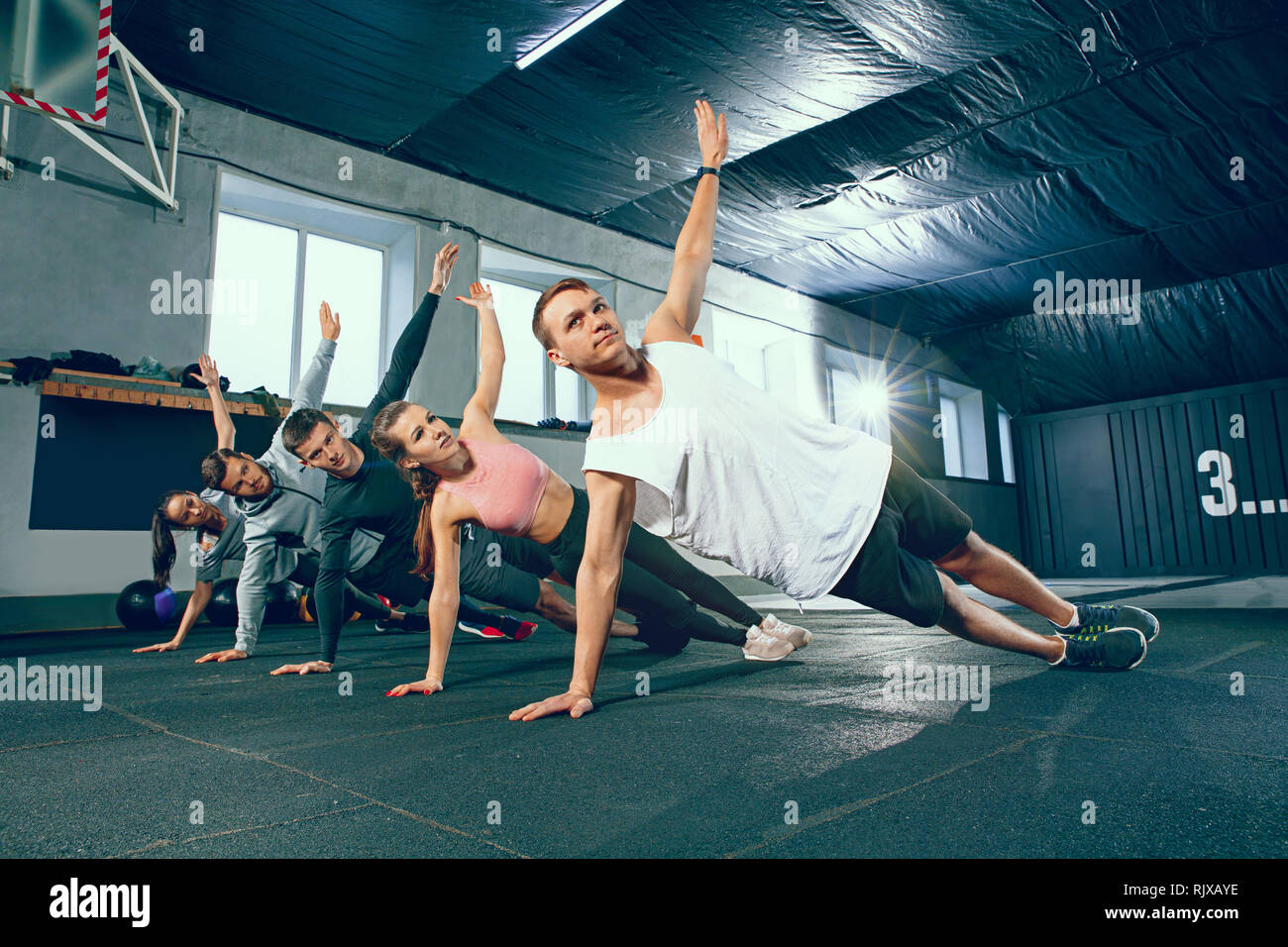 Shot of young men and women standing in plank position at the gym ...