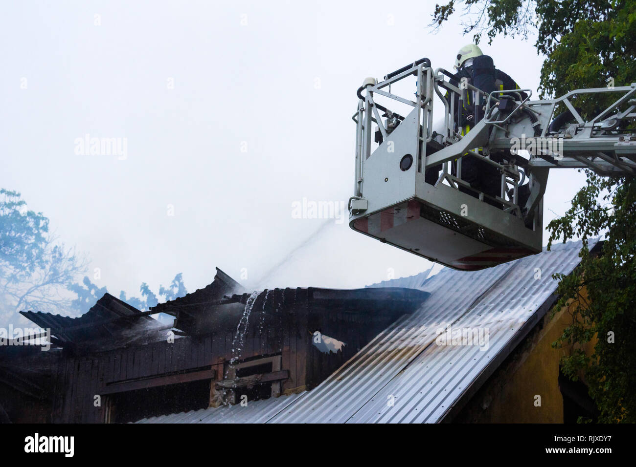 Fire fighter extinguishing flames on burning roof Stock Photo - Alamy