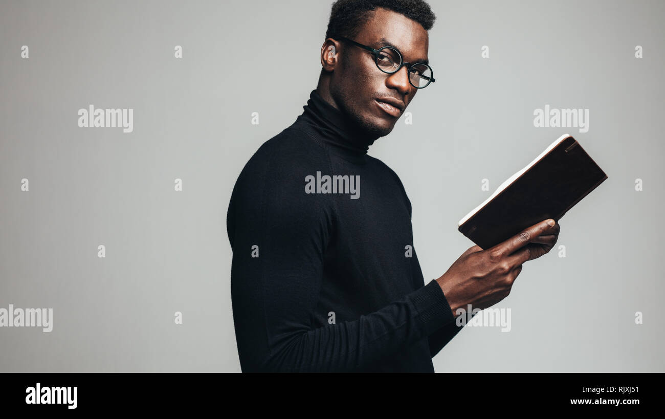 Handsome african man with a book looking at camera. Young guy reading a ...