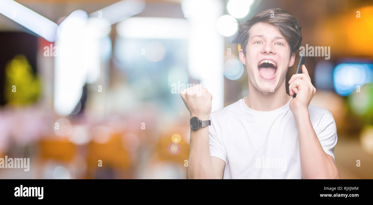 Young man talking on smartphone over isolated background screaming ...