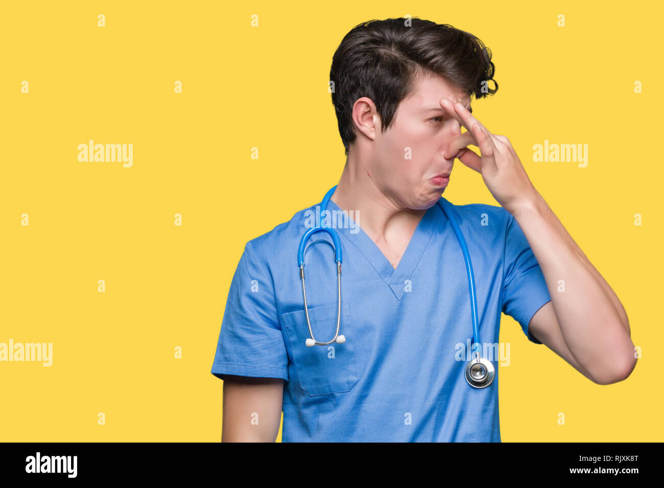 Young doctor wearing medical uniform over isolated background smelling ...