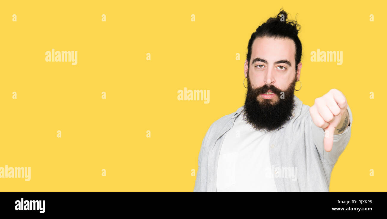 Young man with long hair, beard and earrings looking unhappy and angry ...