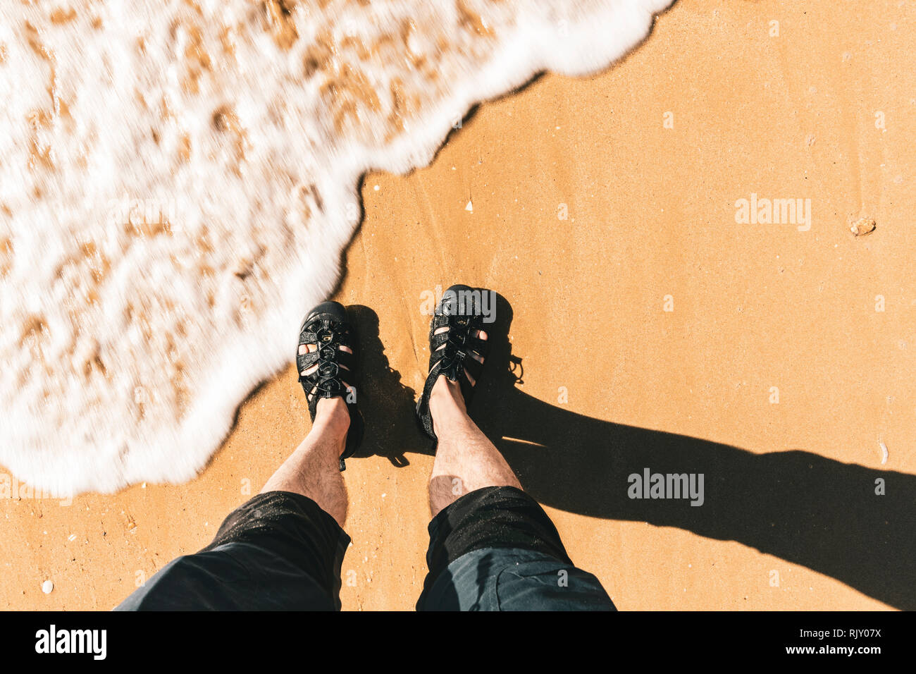 High angle view of mans feet paddling by waters edge on beach ...