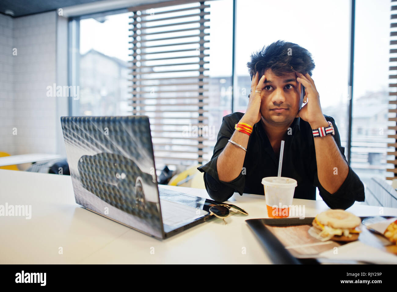 Disappointed and shocked indian man sitting at fast food cafe against ...