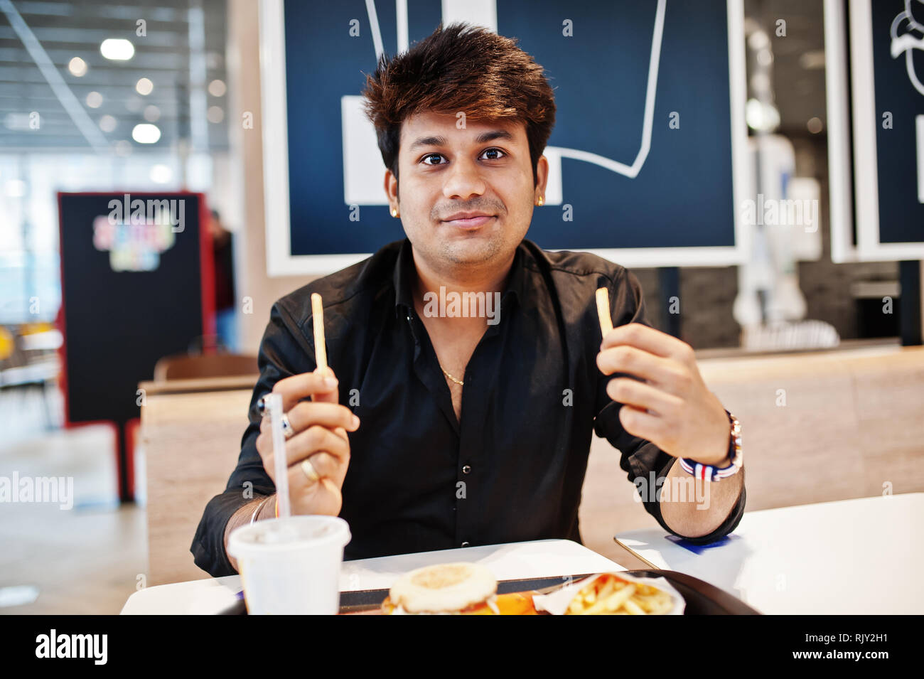 Stylish indian man sitting at fast food cafe and eating french fries ...