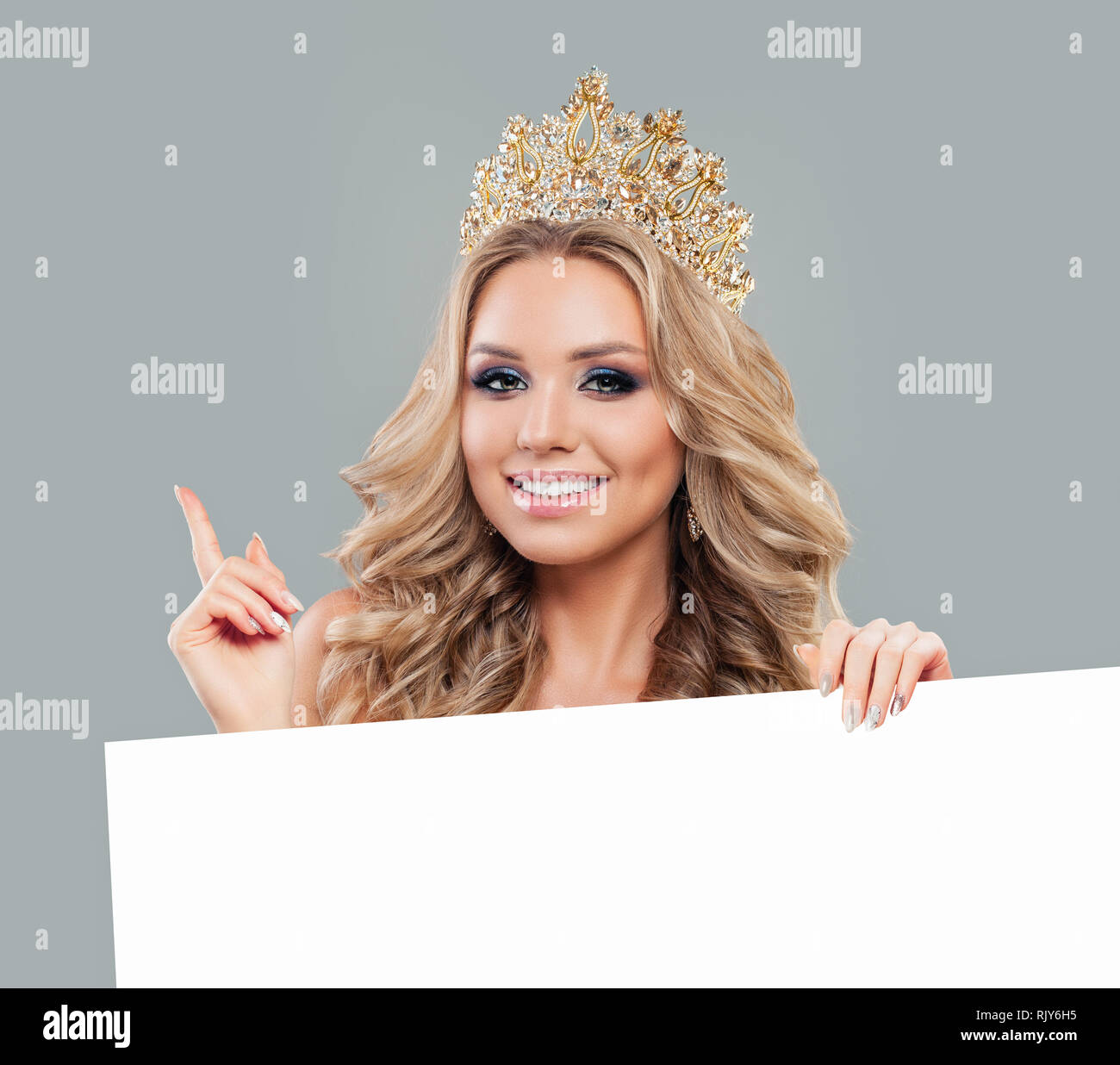 Glamorous woman smiling, pointing up and holding white empty paper ...
