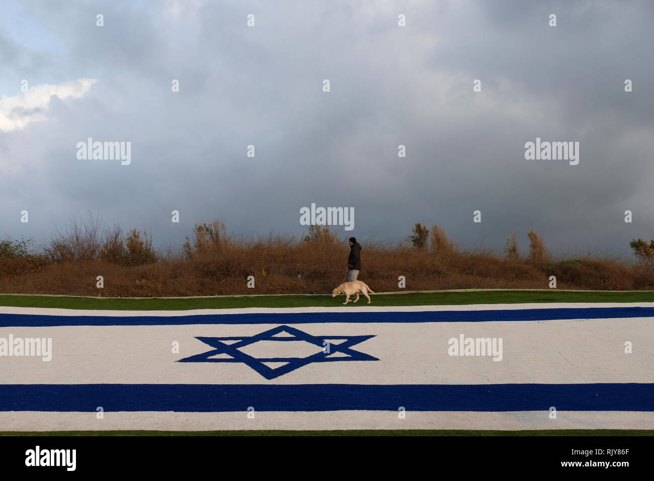 An Israeli civilian walks past with his dog an Israeli flag made of ...