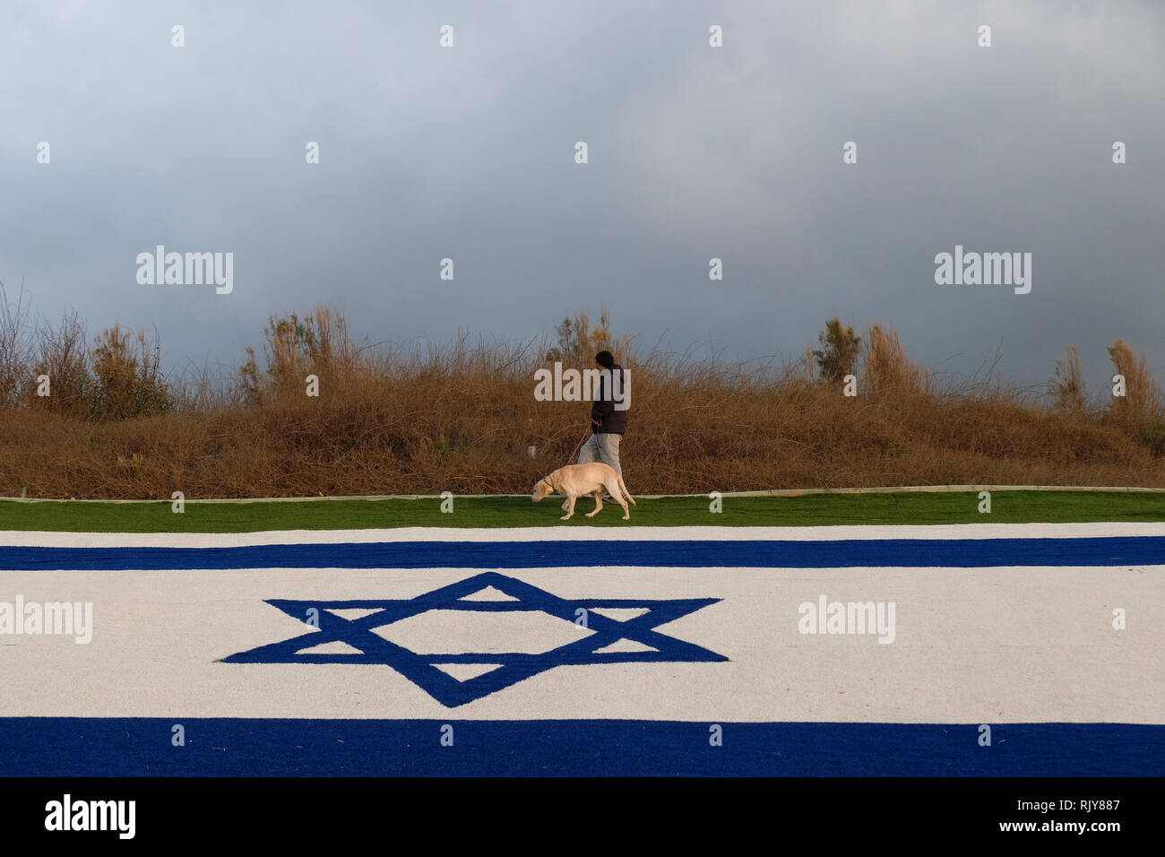 An Israeli civilian walks past with his dog an Israeli flag made of ...