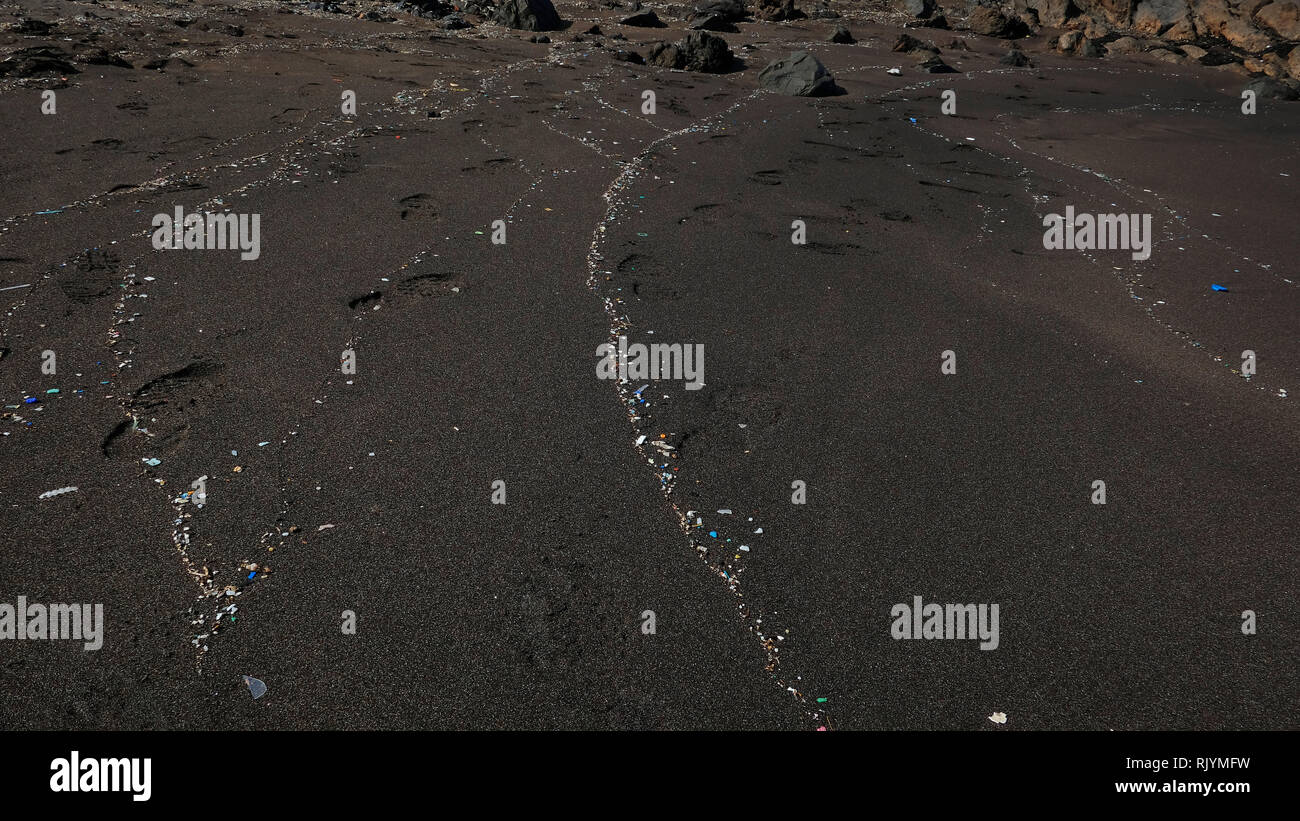 Plastic particles washed up by the waves on a beautiful black sand ...