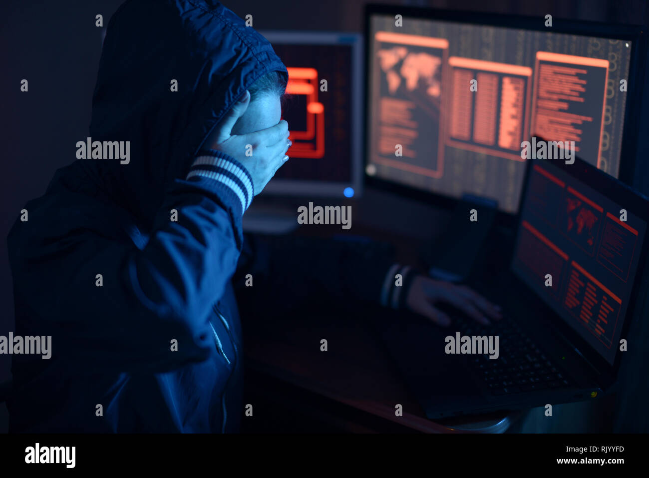 An anonymous girl hacker covers her face with hand while committing a ...