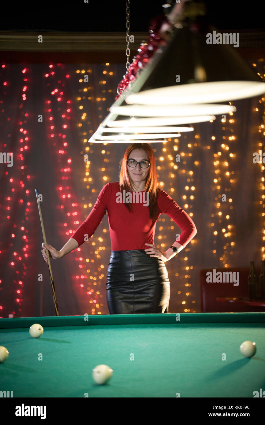 An attractive woman standing in billiard club holding a cue. Posing for ...
