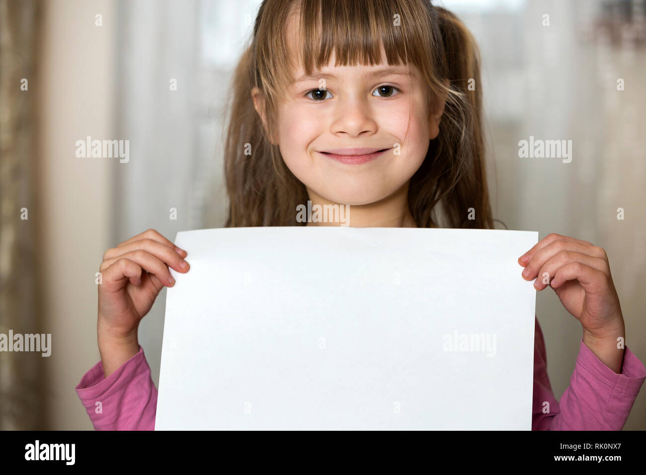 Happy smiling cute child girl holding white copy space sheet of drawing ...