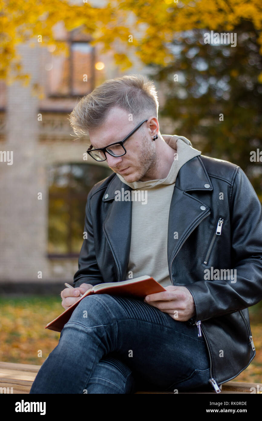 Guy writer in casual clothes makes notes in a notebook and sits on a ...